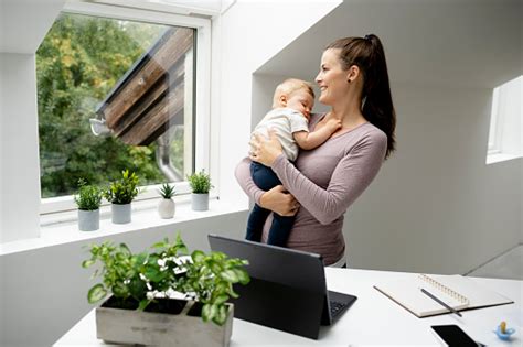 예쁜 젊은 여성 사업가가 직장 책상에 서서 잠자는 아들을 품에 안고 노트북 스마트 폰으로 작업합니다 2명에 대한 스톡 사진 및 기타 이미지 Istock