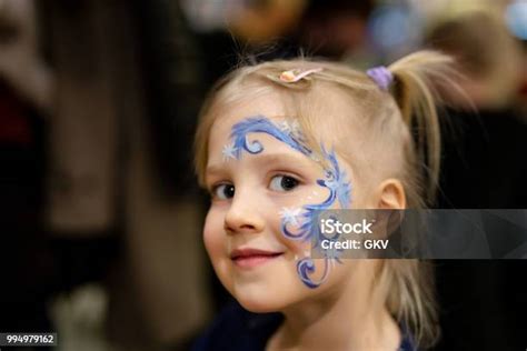 페이스 페인팅으로 귀여운 작은 금발 소녀 아이 얼굴에 수채화로 블루 추상 눈송이 패턴입니다 화려한 그림을 가진 사랑 스러운 아이입니다 어린이 파티 엔터테인먼트 메이크업