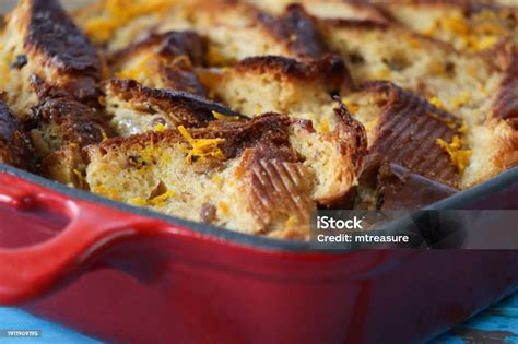 겹겹이 쌓인 빵과 버터 푸딩의 조리된 재료가 포함된 빨간색 베이킹 접시의 전체 프레임 이미지 말린 과일과 강판에 간 오렌지 껍질이 뿌려진 버터를 바른 흰 빵 층의 조각