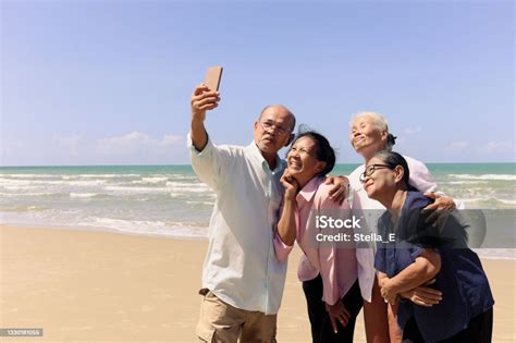 함께 야외를 여행하는 네 명의 노인 선배 친구 그룹은 휴대 전화로 셀카를 찍고 재미있게 보내고 모래 해변에서 시간을 보내고 휴가 휴가를 쉬고 휴식을 취하십시오 60 64세에