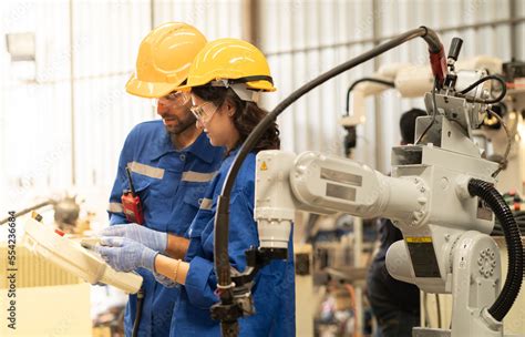 Male Industrial Engineer Using Remote Control Board To Check Robotic Welder Operation In Modern