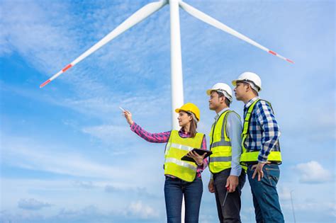 3명의 남녀 엔지니어로 구성된 팀이 태블릿 워키토키를 들고 헬멧과 조끼를 입고 목적지를 가리킵니다 건설 산업 비즈니스 미팅 에너지 풍력 터빈이 있습니다 건축물에 대한 스톡