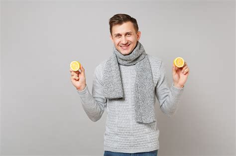 회색 벽 배경 스튜디오 초상화에 고립 회색 스웨터 스카프 레몬을 들고 젊은 남자를 웃 고 건강 패션 라이프 스타일 사람들이 진심으 감정 추운 계절 개념 복사 공간을 비웃는