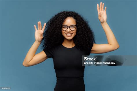 기쁜 여성은 손을 들고 행복하게 움직이고 슬림 한 몸 모양을 가지고 있으며 캐주얼 한 검은 옷을 입고 즐거운 표정을 짓고 푸른 배경에 고립 된 삶을 즐깁니다 사랑스러운 젊은