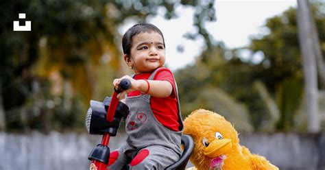 빨간색과 흰색 긴 소매 셔츠를 입은 아이는 노란 곰 봉제 인형과 함께 빨간 자전거를 타고 사진 Unsplash의 무료 인도 이미지