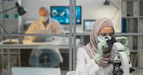 젊은 무슬림 여성 바이러스학자는 실험실에서 남성 동료 네트워킹에 대해 현미경으로 새로운 바이러스의 특성을 연구합니다 사진