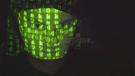 Face Of Male Hacker In Hood Working On A Computer While Green Code Characters Reflect On His