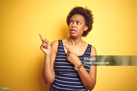 여름 티셔츠를 입은 아프리카 계 미국인 여성이 고립된 노란색 배경 위에 두 손으로 걱정하고 긴장하고 걱정하고 놀란 표정을 지었습니다 T 셔츠에 대한 스톡 사진 및 기타