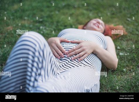 Pregnant White Girl Lies On Green Grass In A Light Striped Dress On A