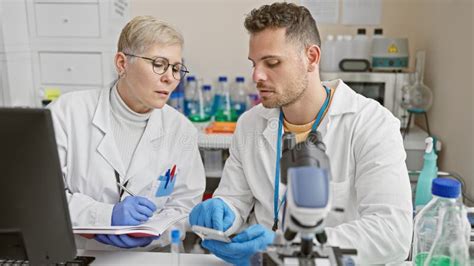A Woman And A Man In Lab Coats Work Collaboratively In A Scientific Laboratory Researching With