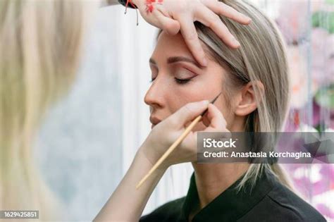 미용실에서 촬영 젊은 아름다운 소녀 모델 마스터 메이크업 아티스트는 눈꺼풀에 그림자를 넣고 눈꺼풀에 컬러 화살표를 그립니다 감정에 대한 스톡 사진 및 기타 이미지 Istock