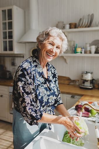 가족 모임에서 맛있고 맛있는 저녁 식사를 요리하기 위해 야채를 준비하는 행복하고 매력적인 노부인의 실내 이미지 창문 앞 부엌에 서서 싱크대에서 양배추를 씻고 껍질을 벗기는