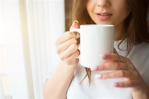 검역 중 부엌에 젊은 여자 흰색 커튼으로 창문에 서서 차나 커피를 마시며 컵을 잡습니다 혼자 마시는 차분한 평화로운 여자 보기를 잘라냅니다 Suggestive Filter에