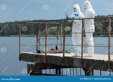 Male Scientist In Protective Suit Pointing On Laptop Screen To Female