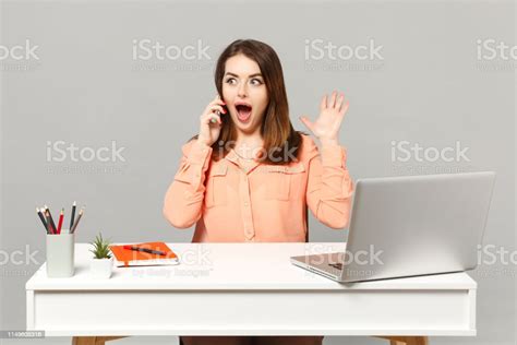 파스텔 캐주얼에 젊은 충격 여자 휴대 전화에 얘기 앉아서 회색 배경에 고립 된 Pc 노트북 책상에서 작동 합니다 성취 비즈니스