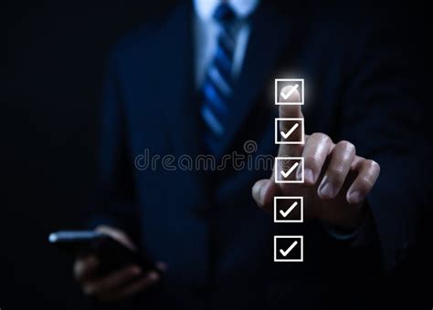 Businessman Hand Holding A Pen Ticking Checkmark On A Box In The List Show On The Virtual Screen