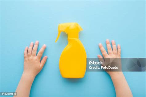 아기 손과 밝은 파란색 테이블 배경에 자외선 차단제의 노란색 스프레이 병 파스텔 색상 더운 여름에 피부 보호에 신경을 쓰십시오 근접 촬영 시점 촬영 하향식 보기 건강관리와
