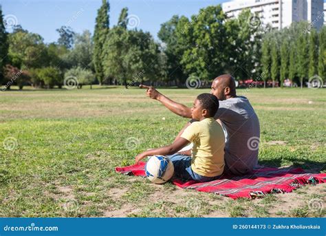 Side View Of Dad And His Son Sitting On Blanket In Park Stock Image