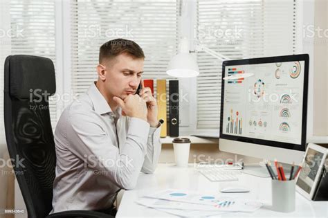 심각 하 고 몰두 비즈니스 휴대 전화에 현대 모니터 컴퓨터 문서 창 배경에 빛 사무실에서 일 얘기과 셔츠는 책상에 앉아 있는 남자 관리자 또는 작업자 합니다 사람들에 대한