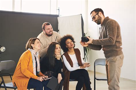 젊은 잘생긴 수염 교육자는 그의 다문화 참석자에게 카메라의 작동 방식을 보여주는 사진 스튜디오 인테리어 강사에 대한 스톡 사진 및 기타 이미지 Istock
