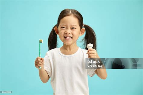 칫솔과 치약 튜브를 들고 흰색 티셔츠를 입고 즐거운 표정을 지고 푸른 고립 된 배경 위에 서서 치아를 청소할 준비를 하는 아름