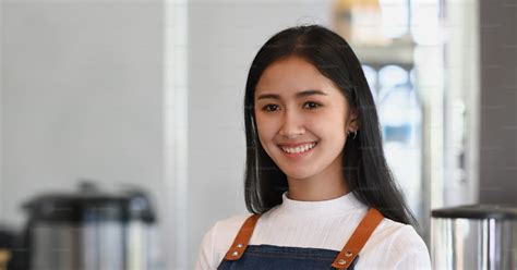 앞치마를 두른 웃는 젊은 여성 기업가의 초상화는 메뉴를 들고 커피숍의 카운터 앞에 서 있다 사진 Unsplash의 커피숍 이미지