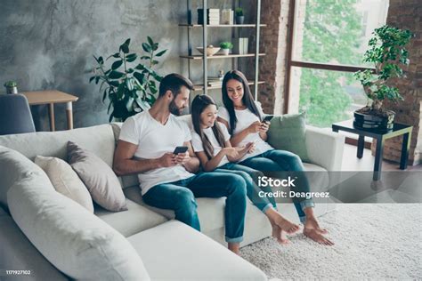 산업 로프트 스타일의 인테리어 거실에서 5g 앱 브라우징을 사용하여 소파에 앉아 캐주얼 흰색 티셔츠 청바지를 입고 좋은 사랑스러운 쾌활한 쾌활한 사랑스러운 건강한 가족