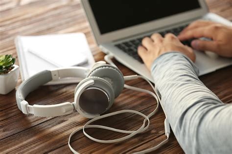 Premium Photo Man Typing On Laptop Headphones And Phone On Wooden Table