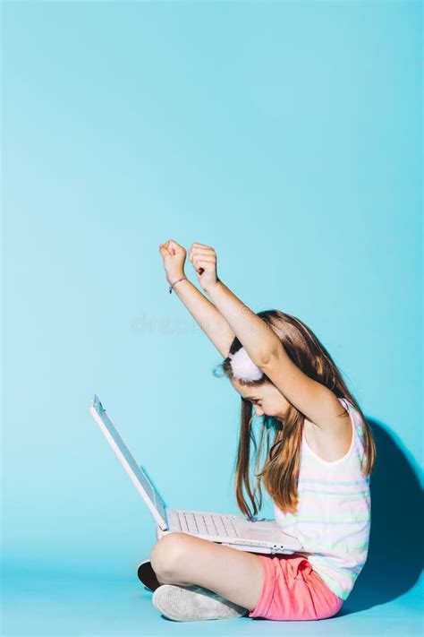 Маленькая девочка с компьтер книжкой на ее коленях поднимая ее руки вверх Стоковое Изображение