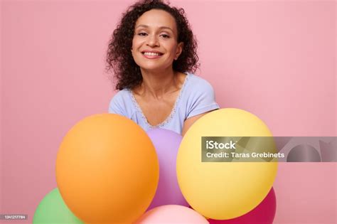 중년 친쾌한 아프리카 계 미국인 여성은 복사 공간으로 분홍색 배경에 팽창 풍선으로 포즈를 취하고 카메라를 바라보며 이빨같은 미소를 짓고 있습니다 스튜디오 샷 의 아름다운