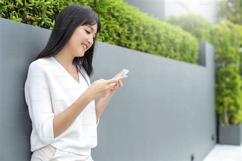 매력적인 아시아 긴 검은 머리 캐주얼 드레스 Tootly 미소 손 사용 스마트 폰의 초상화는 도시 풍경과 하얀 빛 하늘 Copyspace 자유와 쾌활한 감정의 배경을 가지고
