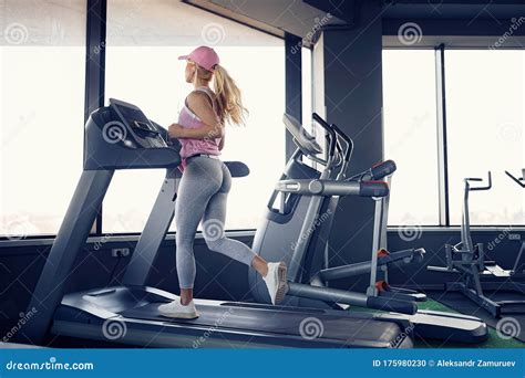 Side View Of Sporty Blonde Woman Exercising On Treadmill In Gym Stock