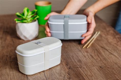 나무 테이블에 탄성 밴드가 있는 두 개의 닫힌 플라스틱 2층 도시락 배경에 도시락 하나를 들고 있는 여성 손 테이블 위의