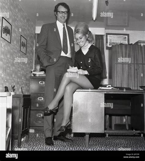 1970s Historical A Secretary Wearing A Mini Shirt Sits On The Edge Of A Desk As She Takes