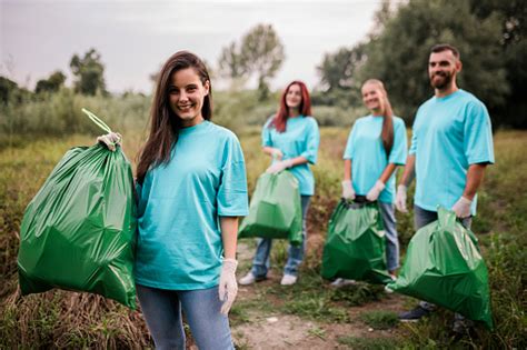 장갑과 쓰레기 봉투를 든 작은 그룹의 자원 봉사자가 방금 청소한 공원에서 멈추는 자연스러운 이미지 청바지와 파란색 티셔츠를 입은 모든 사람들은 지금까지 한 일에 대해