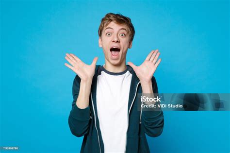 입가를 유지 하는 캐주얼 복장에 놀란 젊은 남자의 초상화는 야자수가 파란색 벽 배경에 고립 된 손을 확산 보여주는 오픈 사람들은 진심으로 감정 라이프 스타일 개념입니다 복사