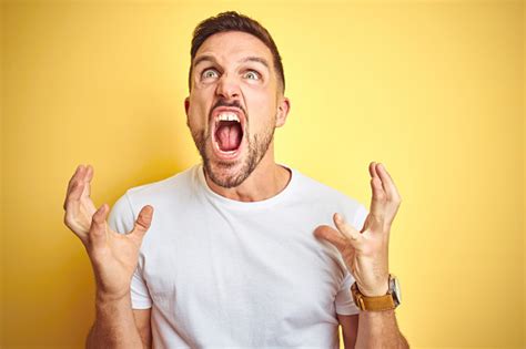 노란색 고립 된 배경에 캐주얼 흰색 티셔츠를 입고 젊은 잘생긴 남자는 미친 미친 소리와 공격적인 표정과 팔을 제기 고함 좌절 개념입니다 T 셔츠에 대한 스톡 사진 및 기타