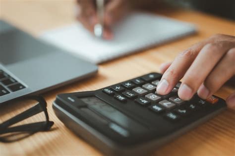 Premium Photo A Businessman Is Using A Calculator And Writing Notes About Cost Analysis At A