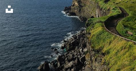 낮에는 파란색과 흰색 흐린 하늘 아래 바다 옆 산에 푸른 잔디 밭 사진 Unsplash의 무료 제주 이미지