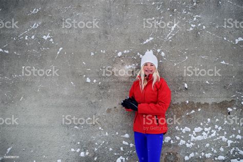 눈이 내리는 겨울에 야외에서 콘크리트 벽에 서있는 활동적인 시니어 여성 러너가 카메라를 바라보고 있습니다 건강한 생활방식에 대한 스톡 사진 및 기타 이미지 Istock