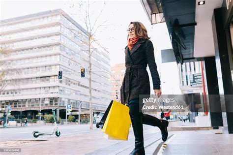 Woman Walking Out Of Store Holding Shopping Bags In City Photo Getty