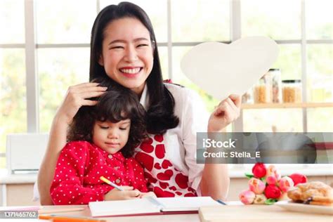 엄마의 무릎에 앉아 어린 아이 딸 소녀 메시지는 빈 하트 모양의 종이를 들고 행복 미소 아름다운 젊은 아시아 엄마 동안 어머니의 날을 축하하기 위해 수제 카드를 준비 아이