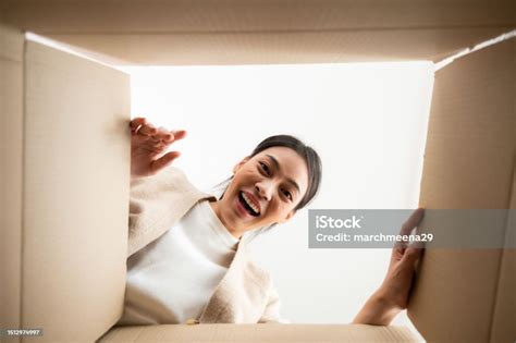 놀란 젊은 아시아 여성이 포장을 풀고 있다 판지 상자를 열고 내부를 들여다봅니다 포장 상자 배달 서비스 인간의 감정과 표정