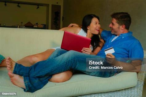 행복 하 고 흥분 젊은 혼합된 인종 몇 아시아 중국 여자와 백인 인터넷 뱅킹 및 신용 카드와 노트북 컴퓨터를 집에서 온라인 쇼핑 소파 2명에 대한 스톡 사진 및 기타 이미지