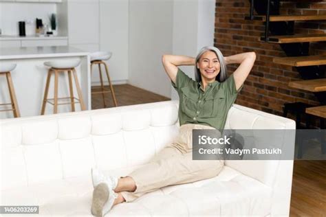 현대 아파트의 소파에 긴 회색 머리카락을 가진 고요한 평온한 중년 여성 머리 뒤에 손을 얹고 뒤로 기대고 노인 여성 휴식 45 49세에 대한 스톡 사진 및 기타 이미지