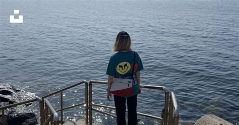 검은 색과 빨간색 재킷을 입은 여자는 수역 근처의 회색 금속 난간에 서 있습니다 사진 Unsplash의 무료 제주 이미지