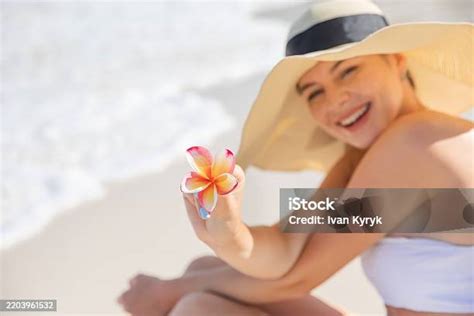 젊은 여자가 해변에서 쉬고 있습니다 행복한 섬 라이프스타일 모자를 쓰고 꽃을 들고 해변에 앉아 있는 소녀 초점이 맞는 꽃 25 29세에 대한 스톡 사진 및 기타 이미지