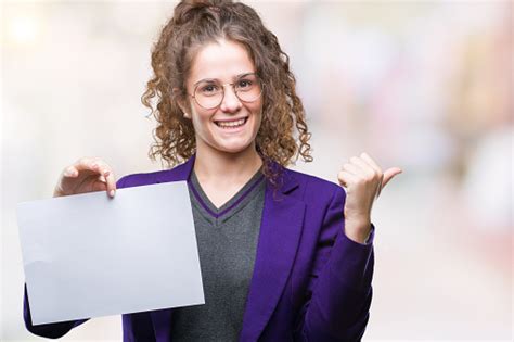 고 행복 얼굴 미소와 측면까지 손가락으로 보여주는 격리 된 배경 위에 빈 종이 들고 교 복을 입고 젊은 갈색 머리 학생 소녀 가리키기에 대한 스톡 사진 및 기타 이미지