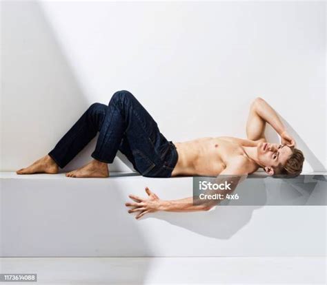 전체 길이 한 남자 만 사이드 뷰 프로필 보기 2029 세 성인 잘 생긴 사람들 백인 남성 젊은 남자 그림자 관능 마초 복 근 가슴 청바지를 입고 흰색 배경 앞에 누워몸통