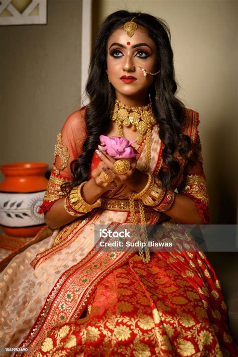 전통적인 사리 골드 주얼리 뱅글을 입은 예쁜 어린 인도 소녀의 초상화가 실내 스튜디오 조명에서 그녀의 손에 꽃을 들고 있습니다 인도 문화 행사 종교 및 패션 20 24세에